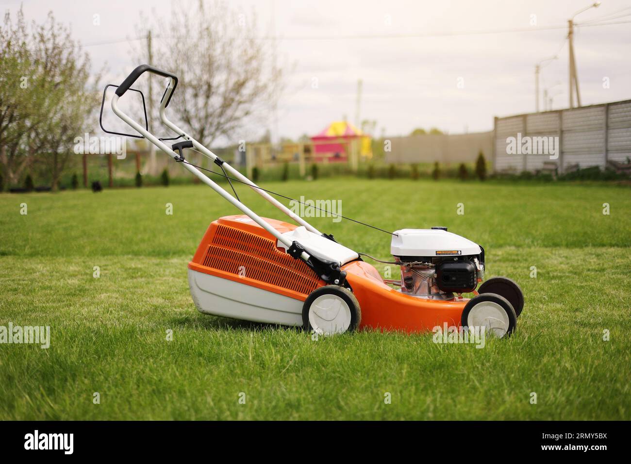side view of modern orange-grey electric lawn mower cutting bright lush ...