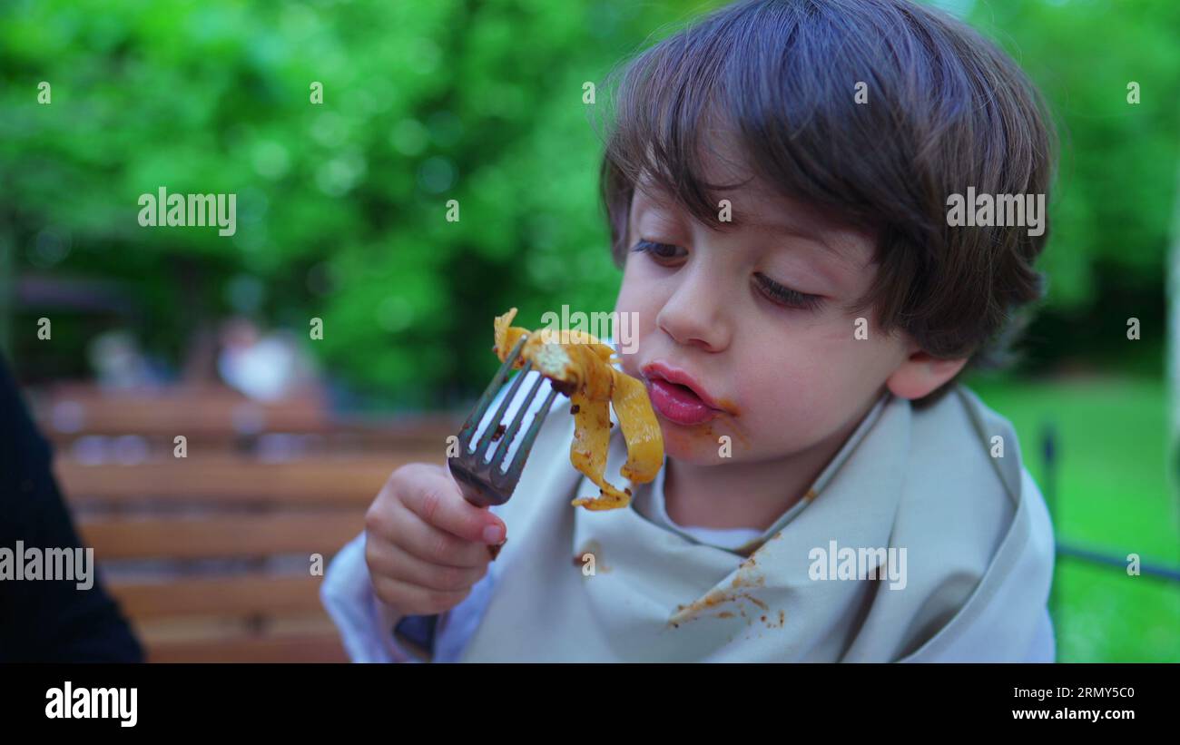 Messy small boy eating pasta for lunch in outdoors sunny setting ...