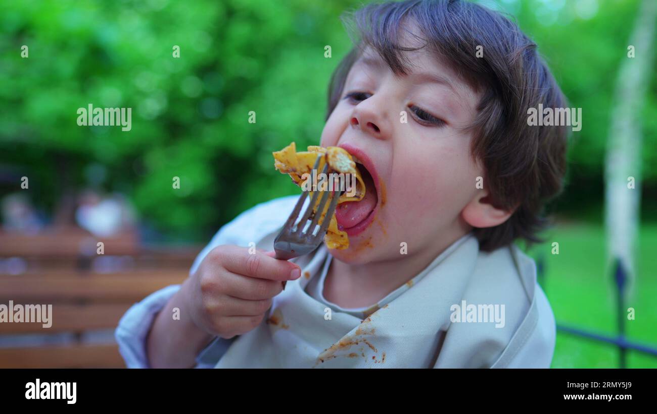Messy small boy eating pasta for lunch in outdoors sunny setting ...