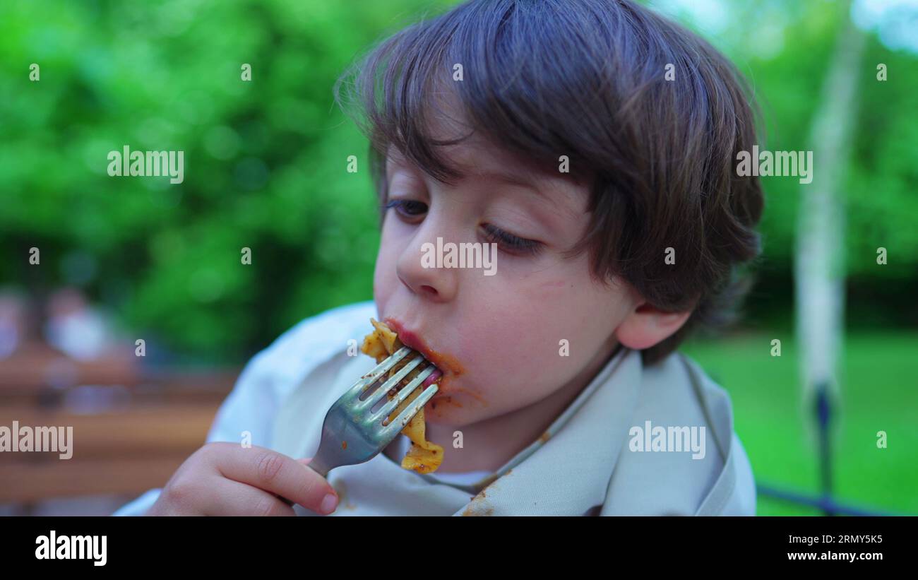 Messy small boy eating pasta for lunch in outdoors sunny setting ...