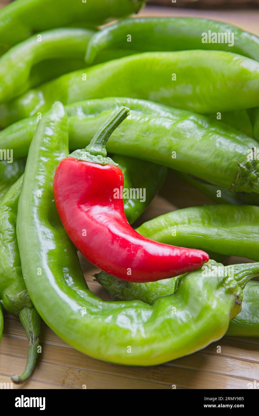 A close up photo of a red pepper sitting on a pile of long green ...