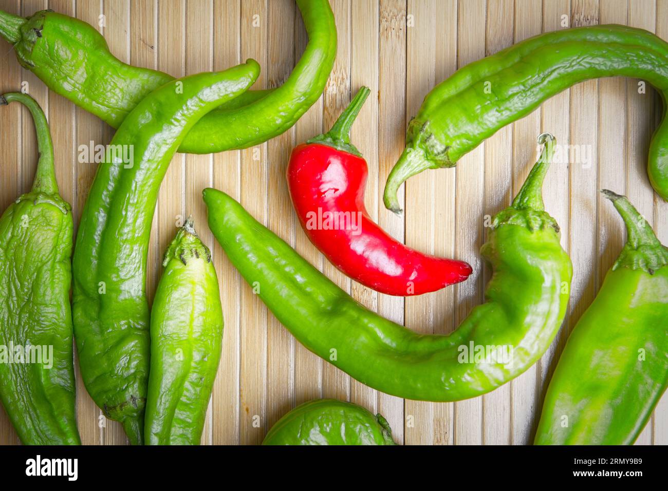 A flat lay photo of long green peppers and a shorter red pepper ...
