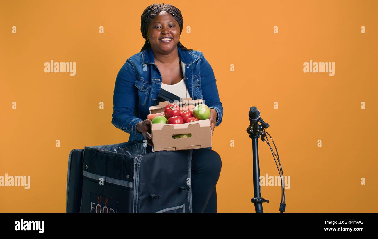 African american courier carefully carrying basket of fruits from food ...