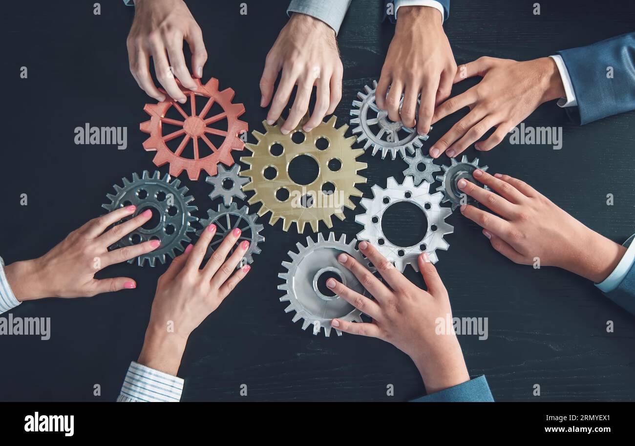 People joining cog wheel on the black desk Stock Photo - Alamy