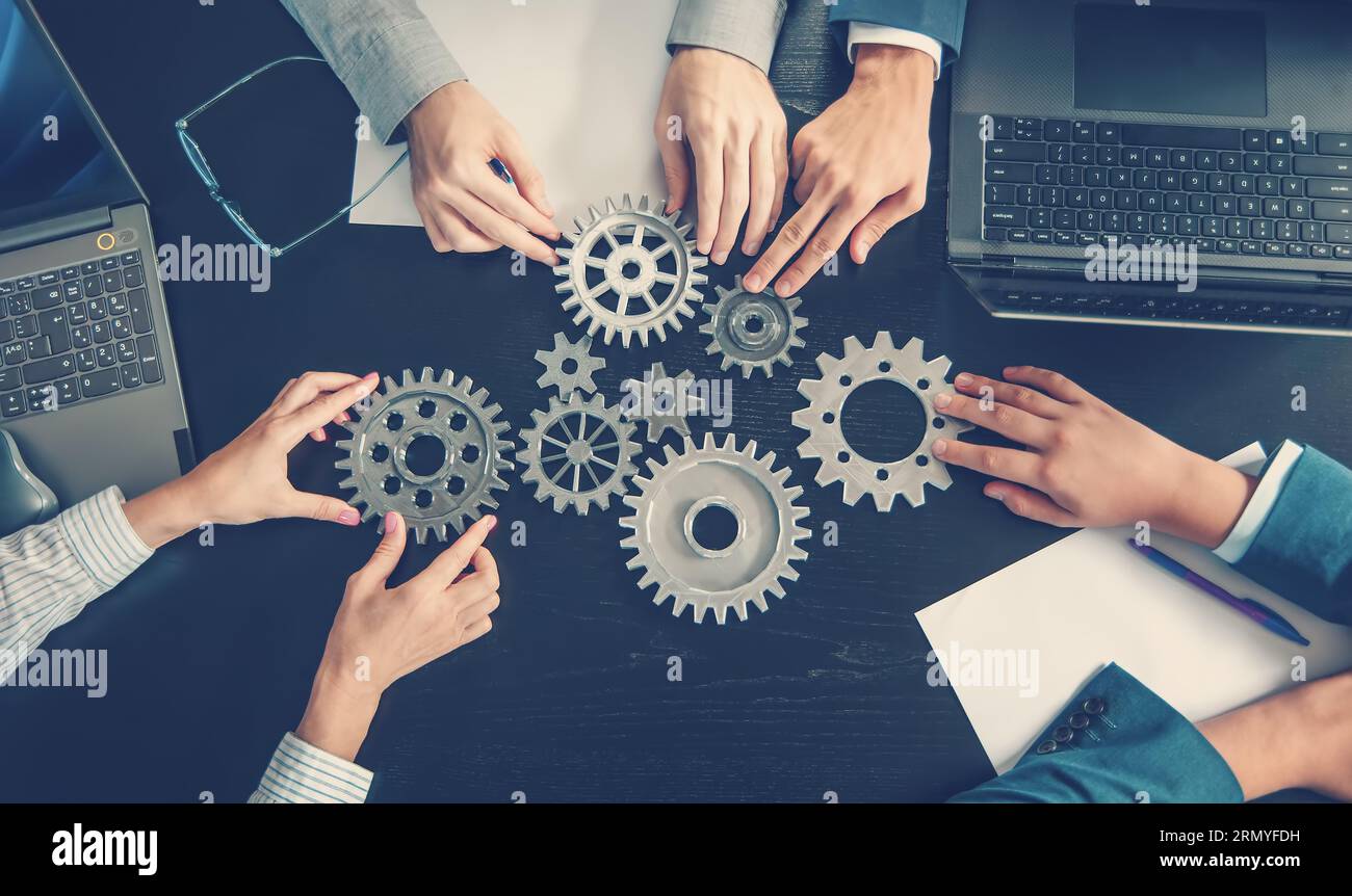 People joining cog wheel on the black desk Stock Photo - Alamy