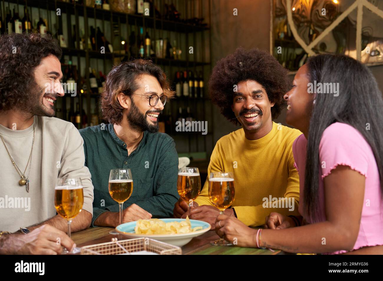 Group of young people drinking beer in a bar. Four multi-ethnic friends ...