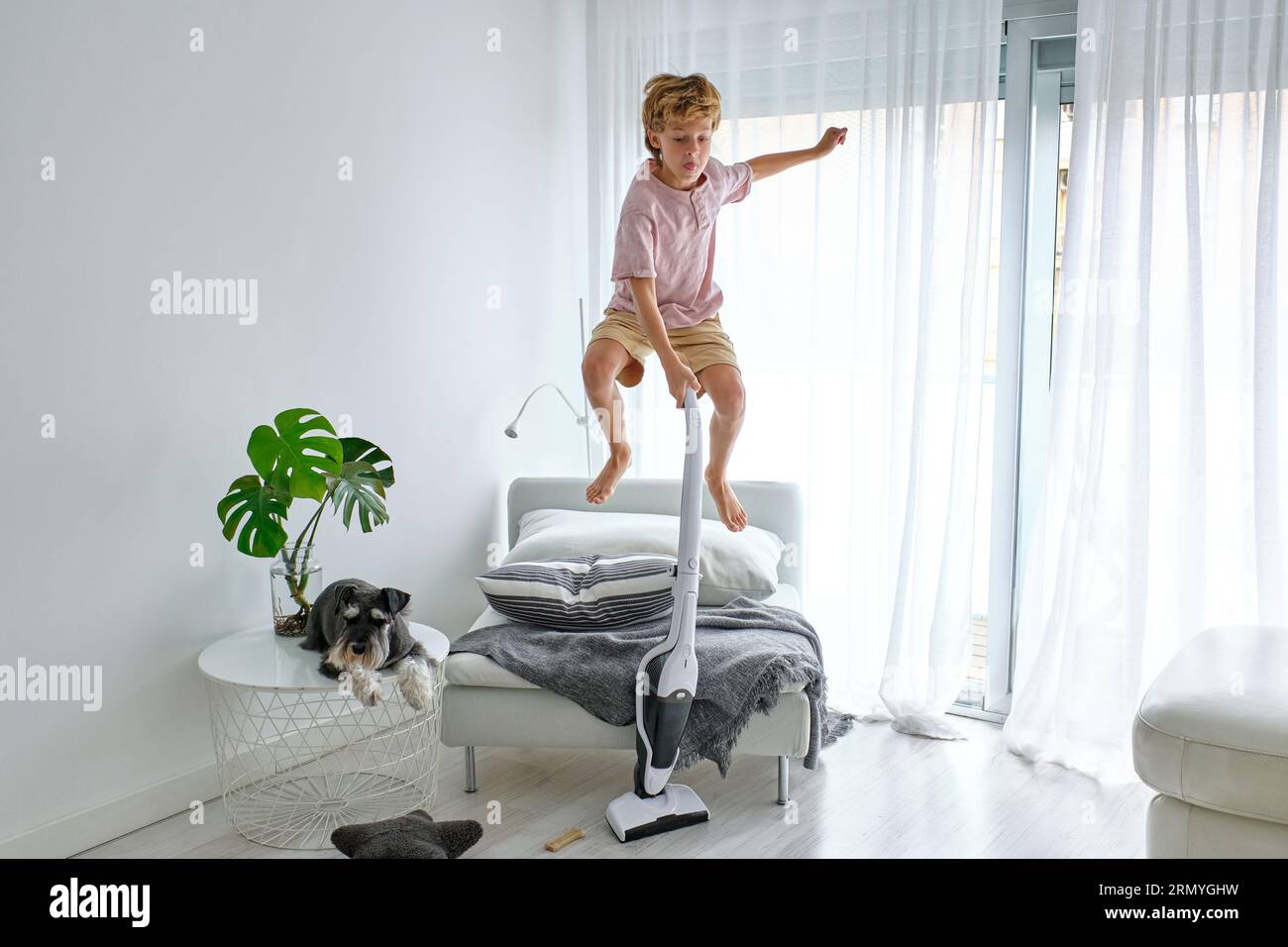 Barefoot boy leaping from chair while tidying floor near table with ...