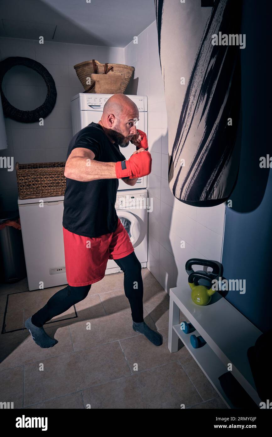 Man training boxing in the laundry room at home with a bag and gloves ...