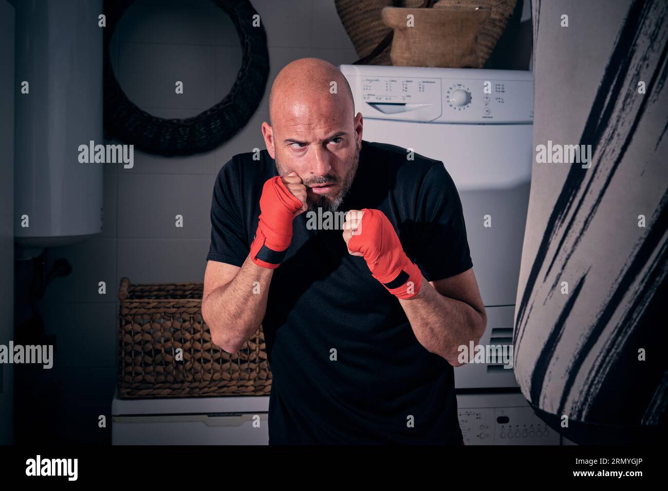 Man training boxing in the laundry room at home with a bag and gloves ...