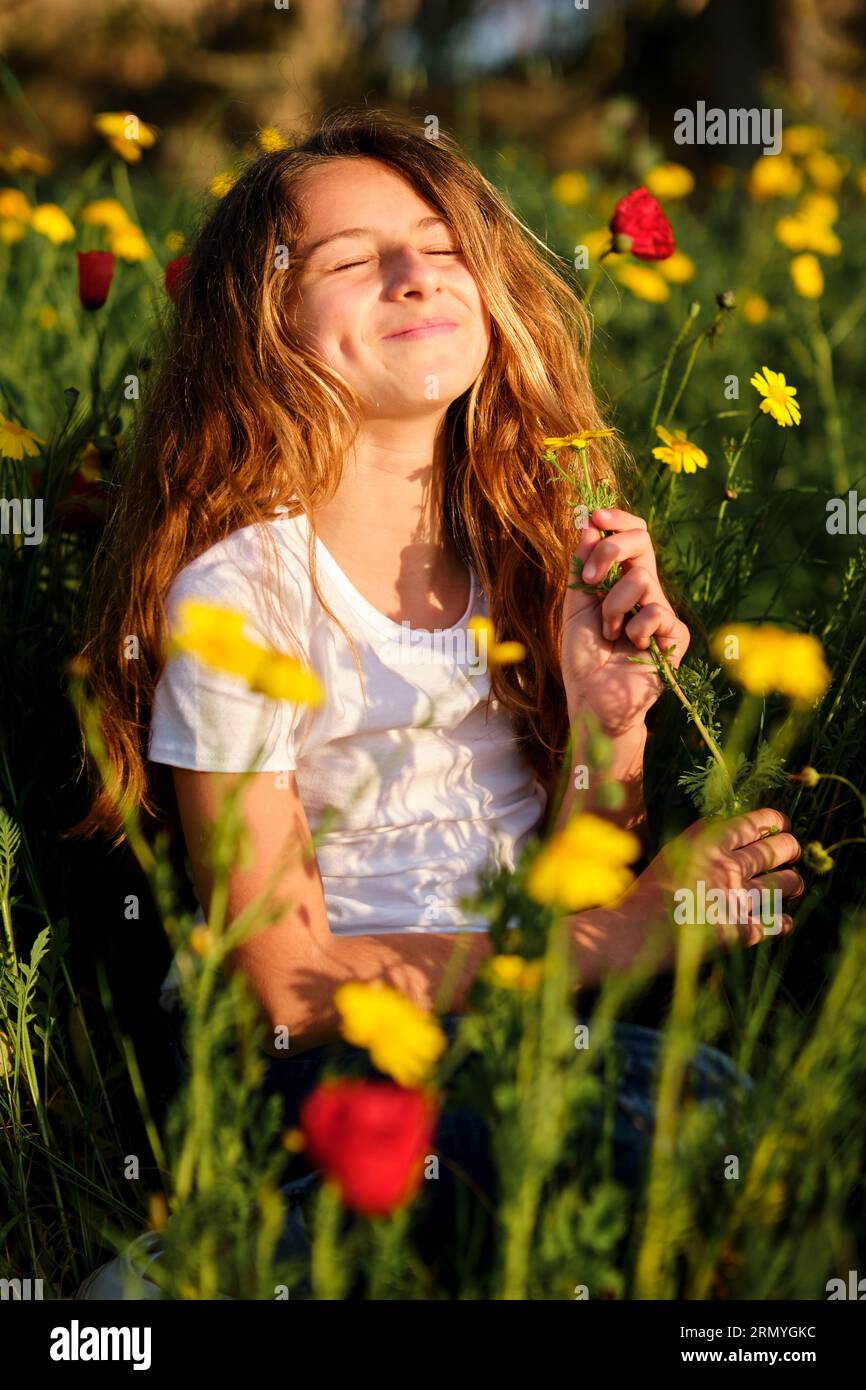 Optimistic girl smiling and smelling fresh flower with closed eyes ...