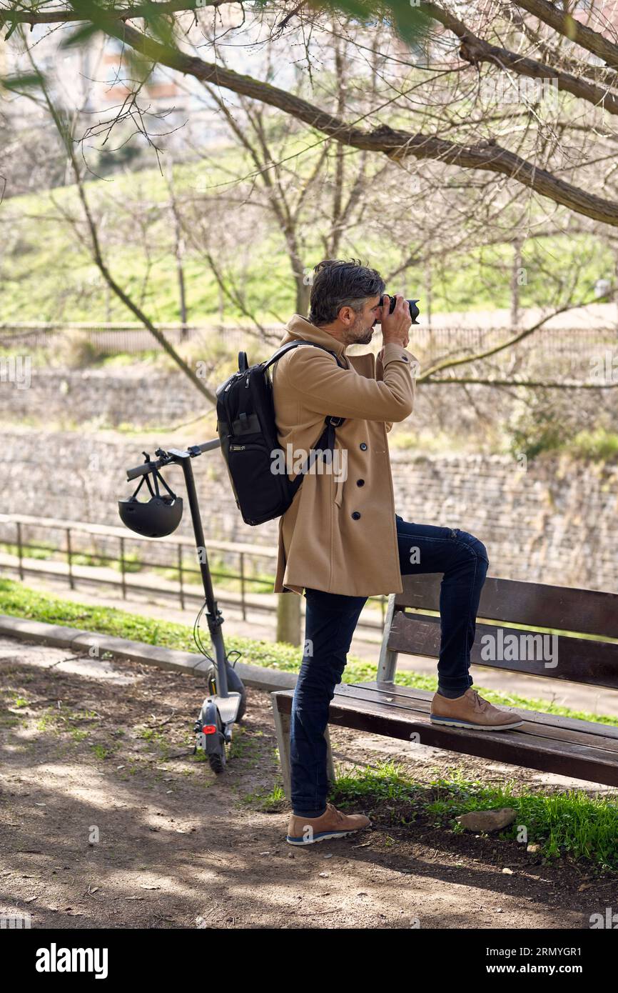 Side view of man standing near electric scooter and taking picture on ...