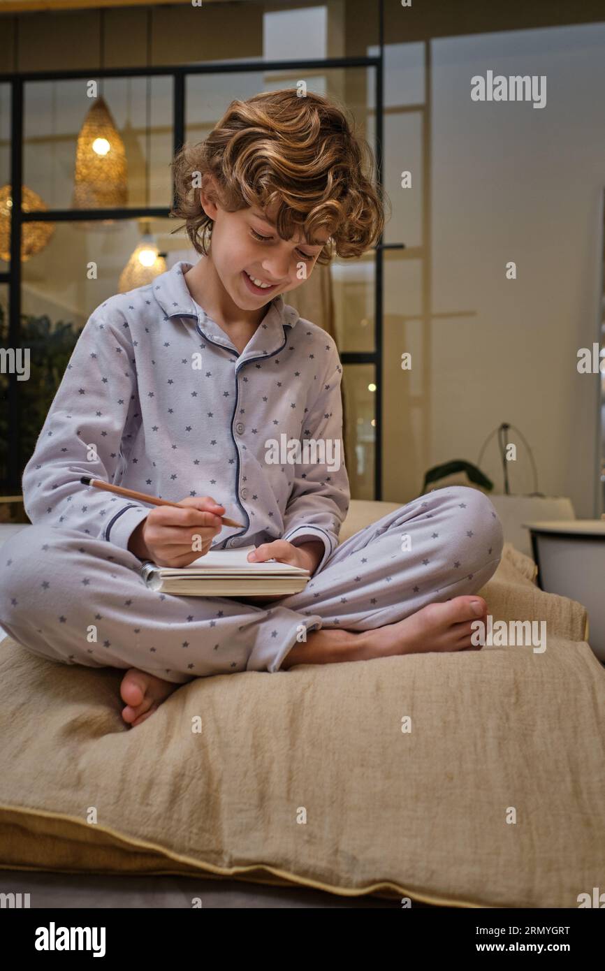 Full body of positive child with curly hair in nightwear writing in ...