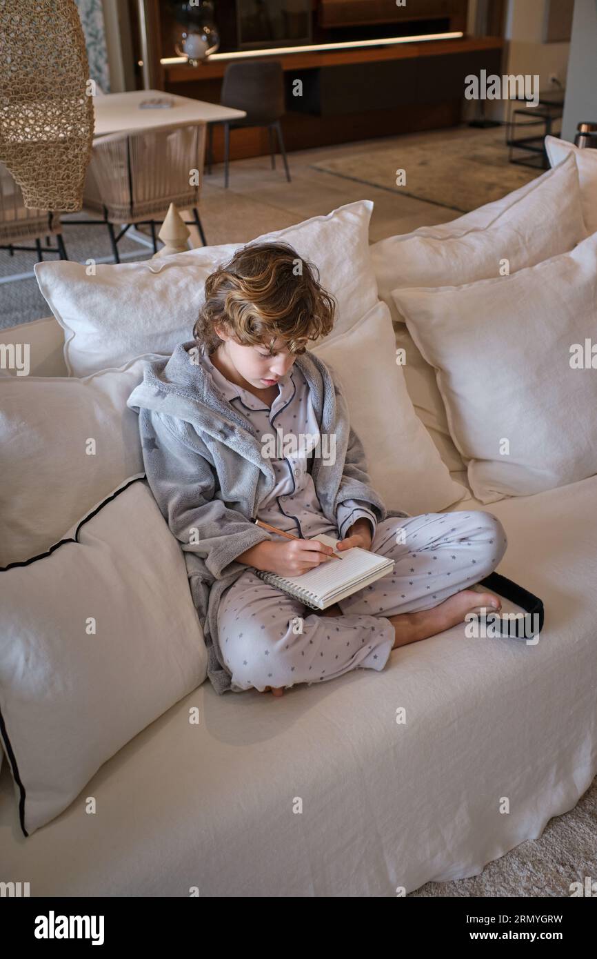 High angle of full length barefoot boy with crossed legs in bathrobe ...