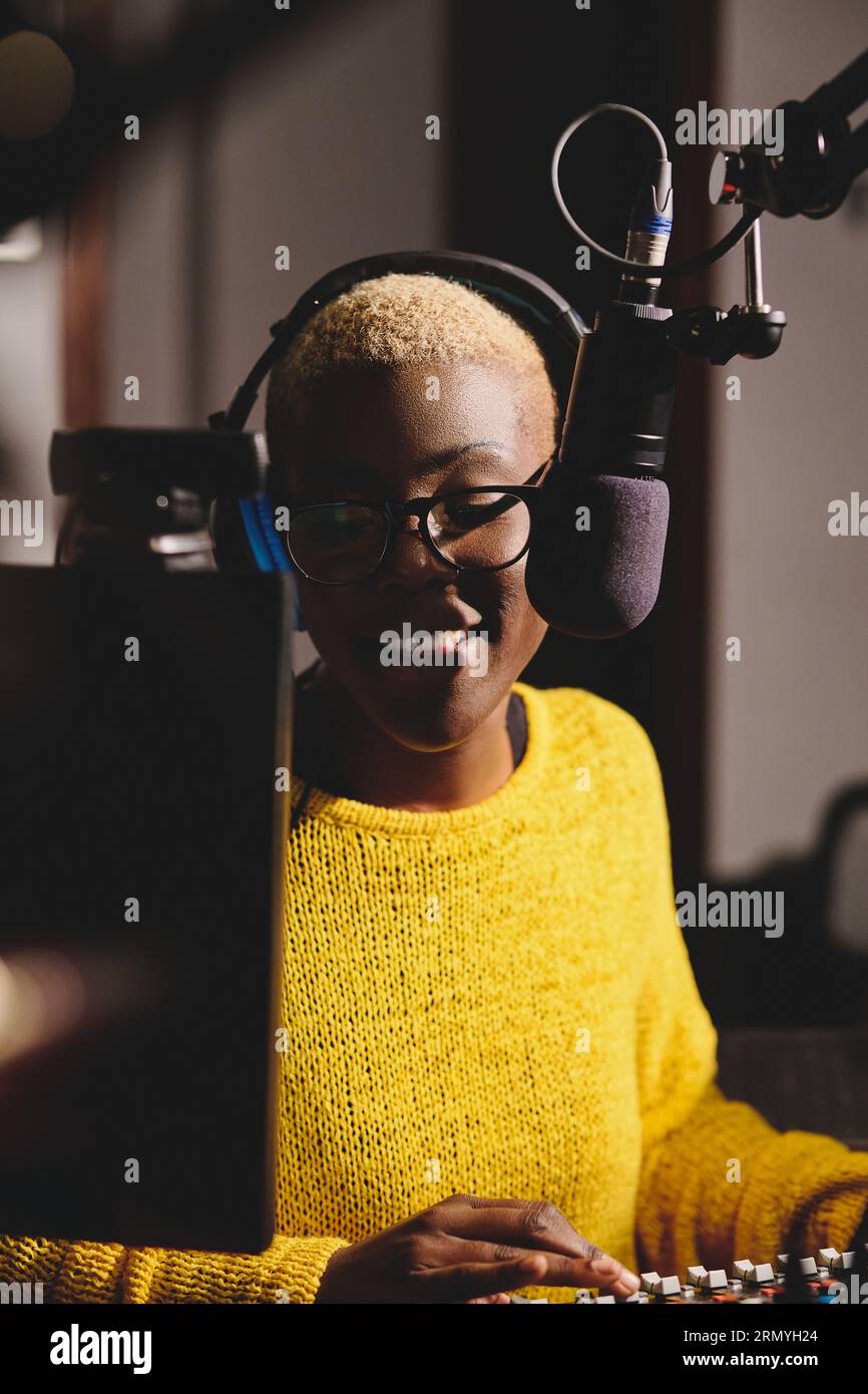 Smiling ethnic female radio host in vivid yellow sweater working in ...