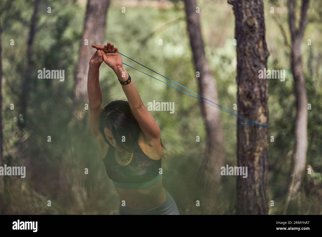 Healthy female raising hands above head while pulling resistance band ...