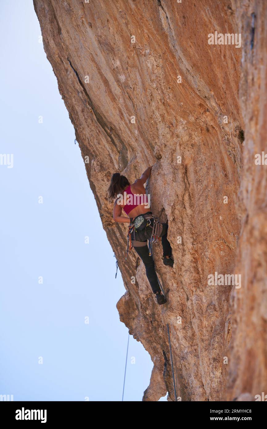 Low angle back view of anonymous female alpinist hanging on rocky steep ...