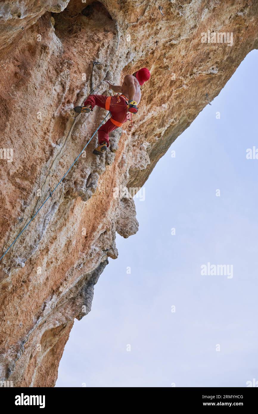 From below back view of unrecognizable alpinist in red clothes climbing ...