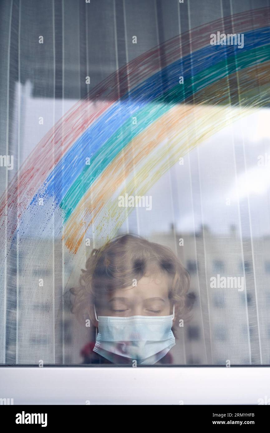 Through glass view of child in protective mask standing alone with eyes ...