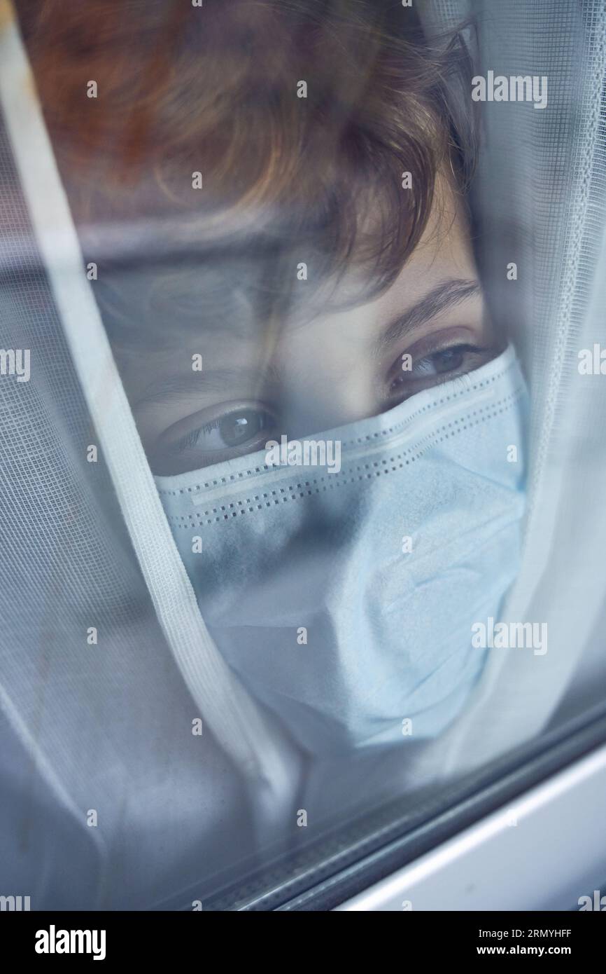 Thoughtful boy with curly hair wearing disposable medical face mask ...