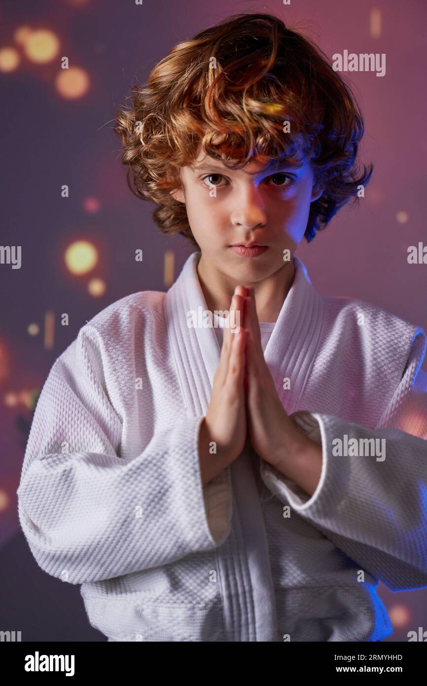 Calm preteen kid in white kimono looking away with folded hands in ...