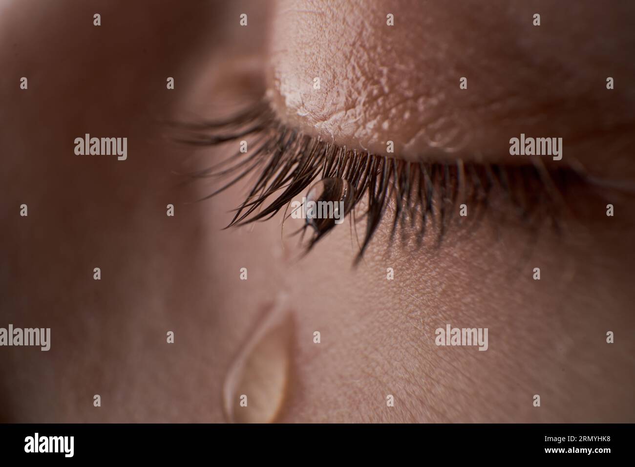 Closeup closed eye of crop anonymous unhappy crying kid with small tear ...