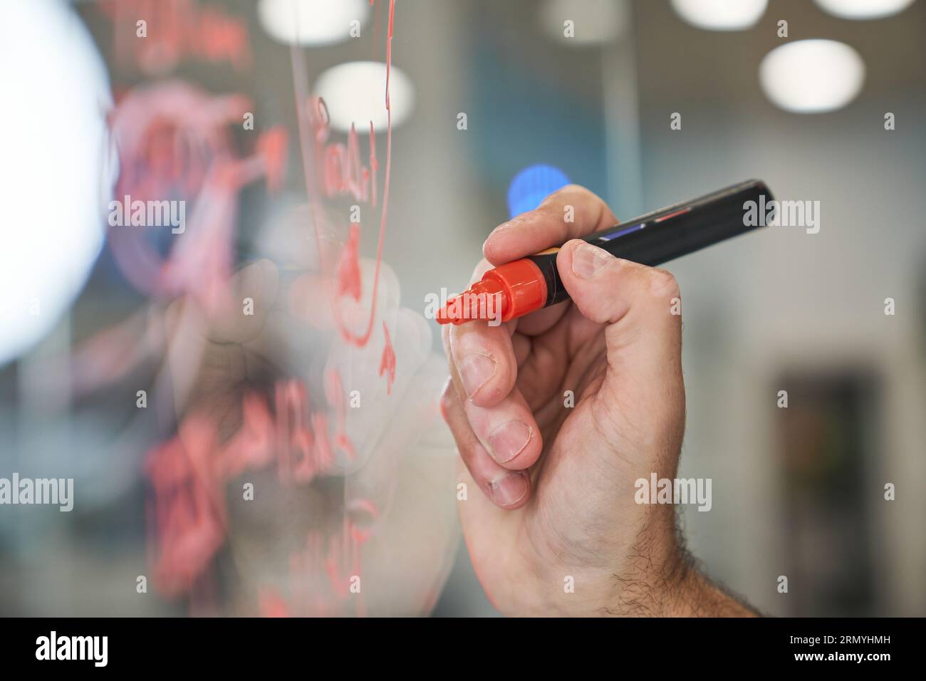 Unrecognizable man drawing on glass board with red marker while ...