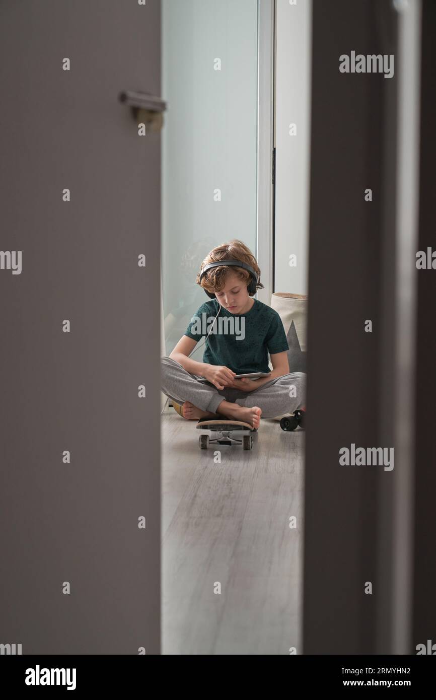 View from doorway of full body barefoot boy in headphones sitting on ...