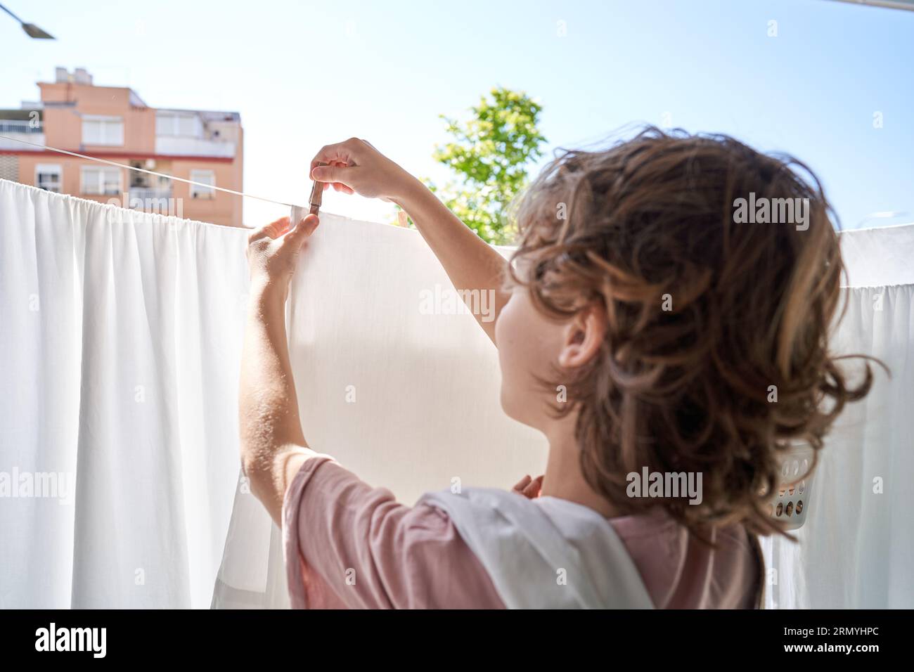 From behind of child with curly hair hanging up sheets on clothesline ...