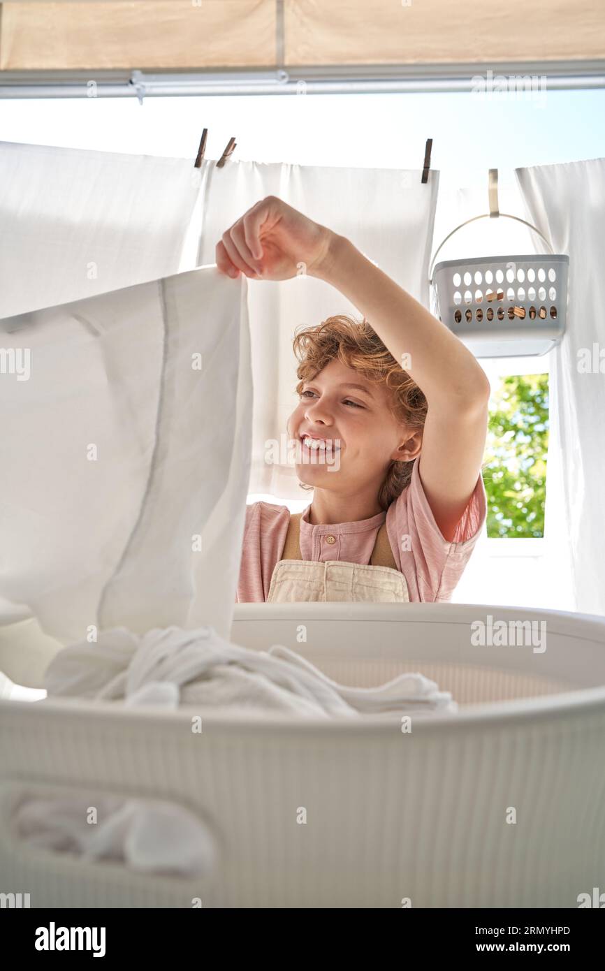 Smiling child standing under clothesline and taking white sheets from ...