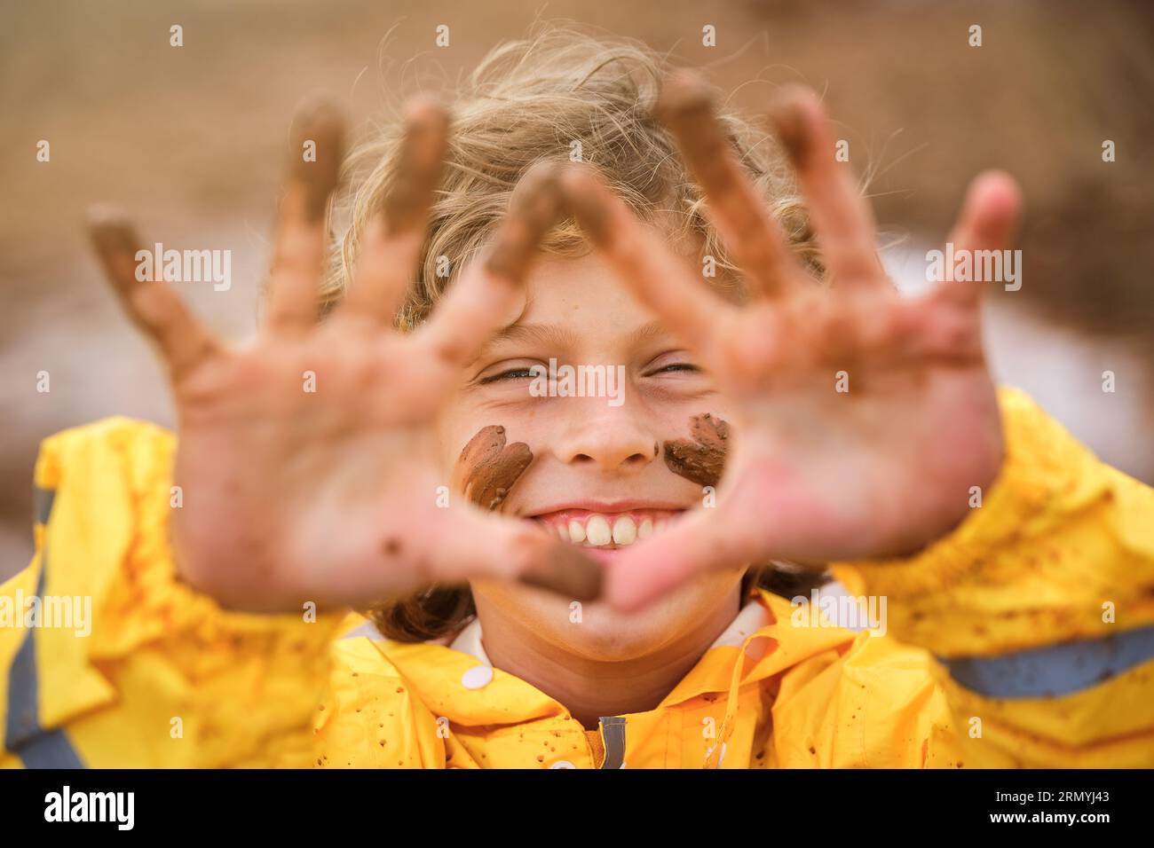 Carefree child with muddy marks on face wearing yellow raincoat looking ...