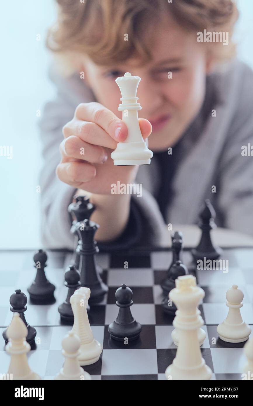 Adorable preteen boy squinting and demonstrating chess piece of queen ...