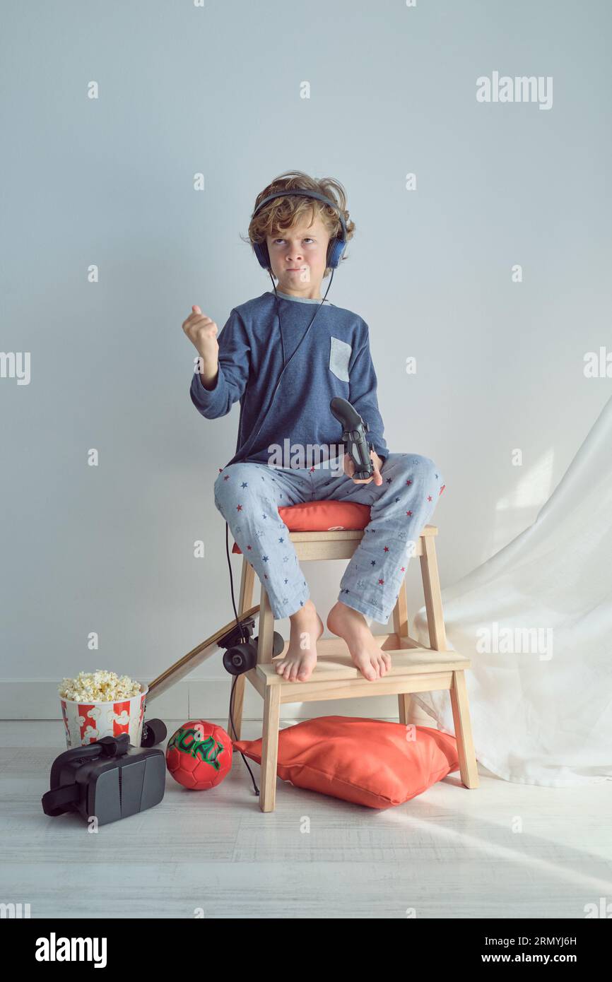 Full body of annoyed kid with blond hair in pajama and headphones ...