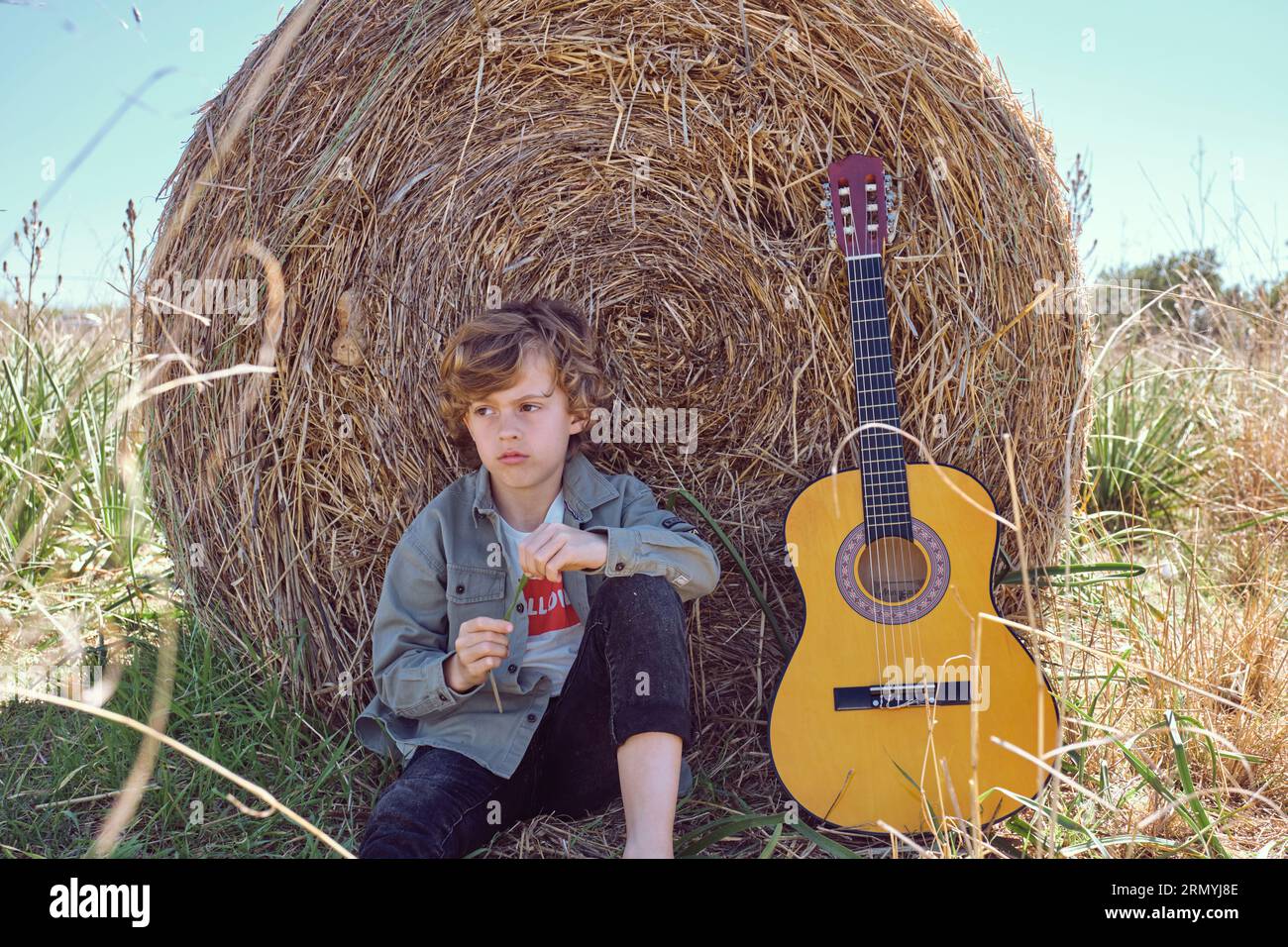 Disappointed curly haired boy sitting near acoustic guitar for hobby ...