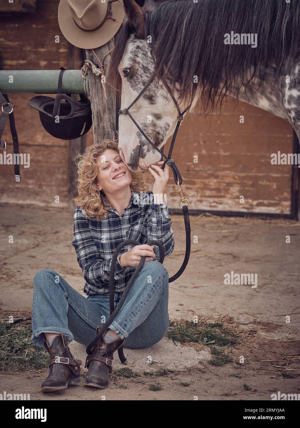 Full body of delighted female equestrian caressing white spotted horse ...