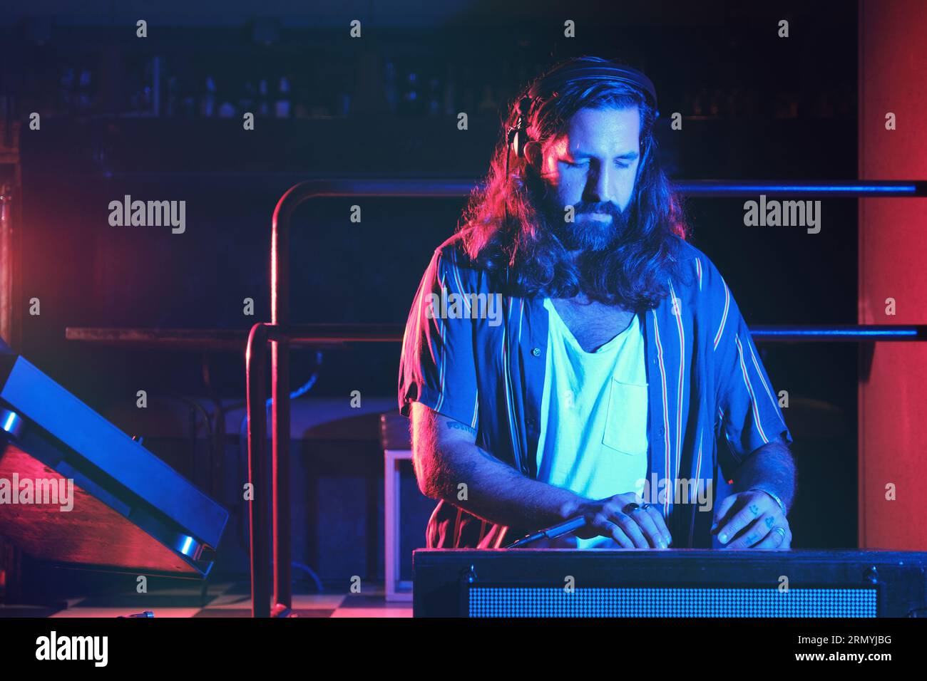 Serious skilled male DJ with beard in casual wear using modern mixer ...