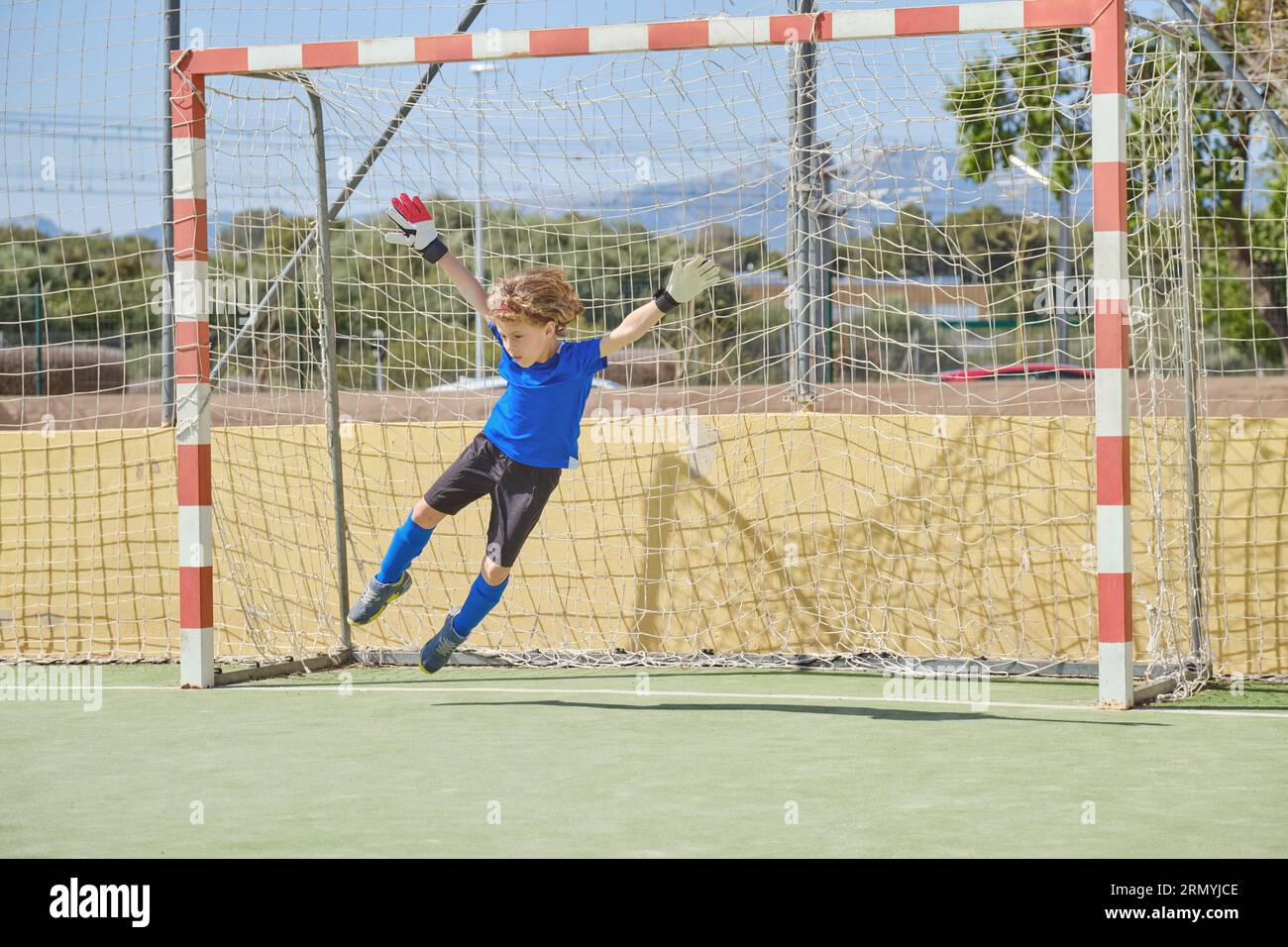 Full body of preteen goalkeeper in sportswear jumping to side while ...