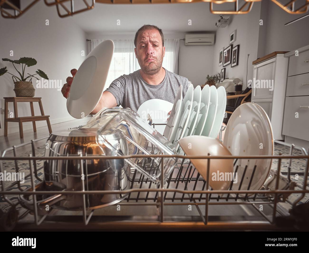 Puzzled man in casual wear unloading modern dishwasher with set of ...