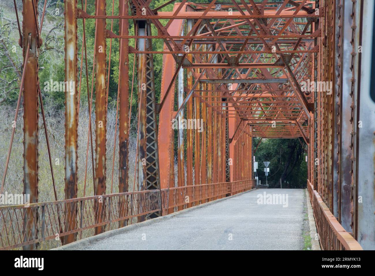 Looking down the roadway on an old red metal bridge. The bridge girders ...