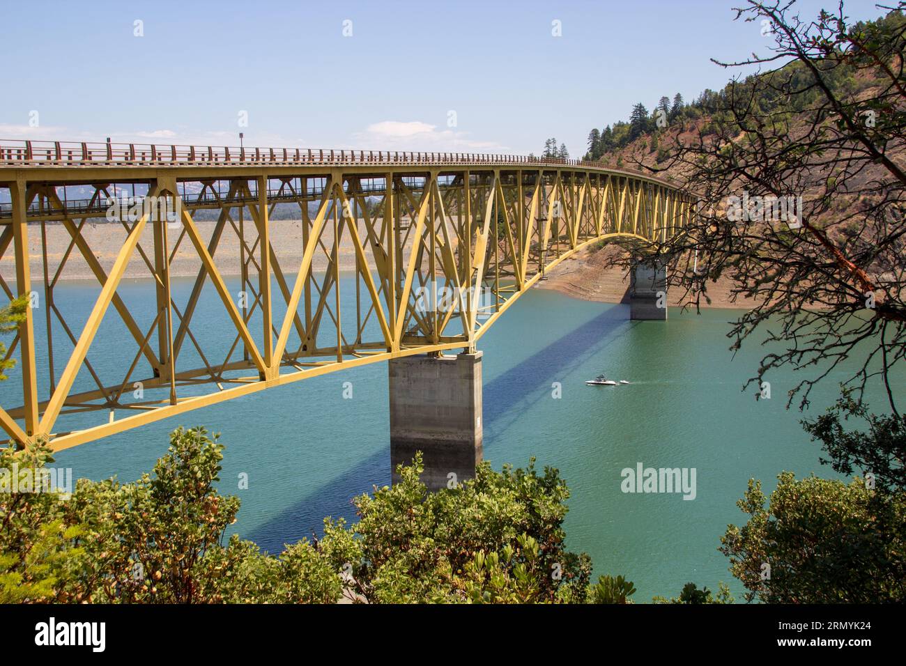 A yellow metal bridge is going across a body of blue green water. The ...