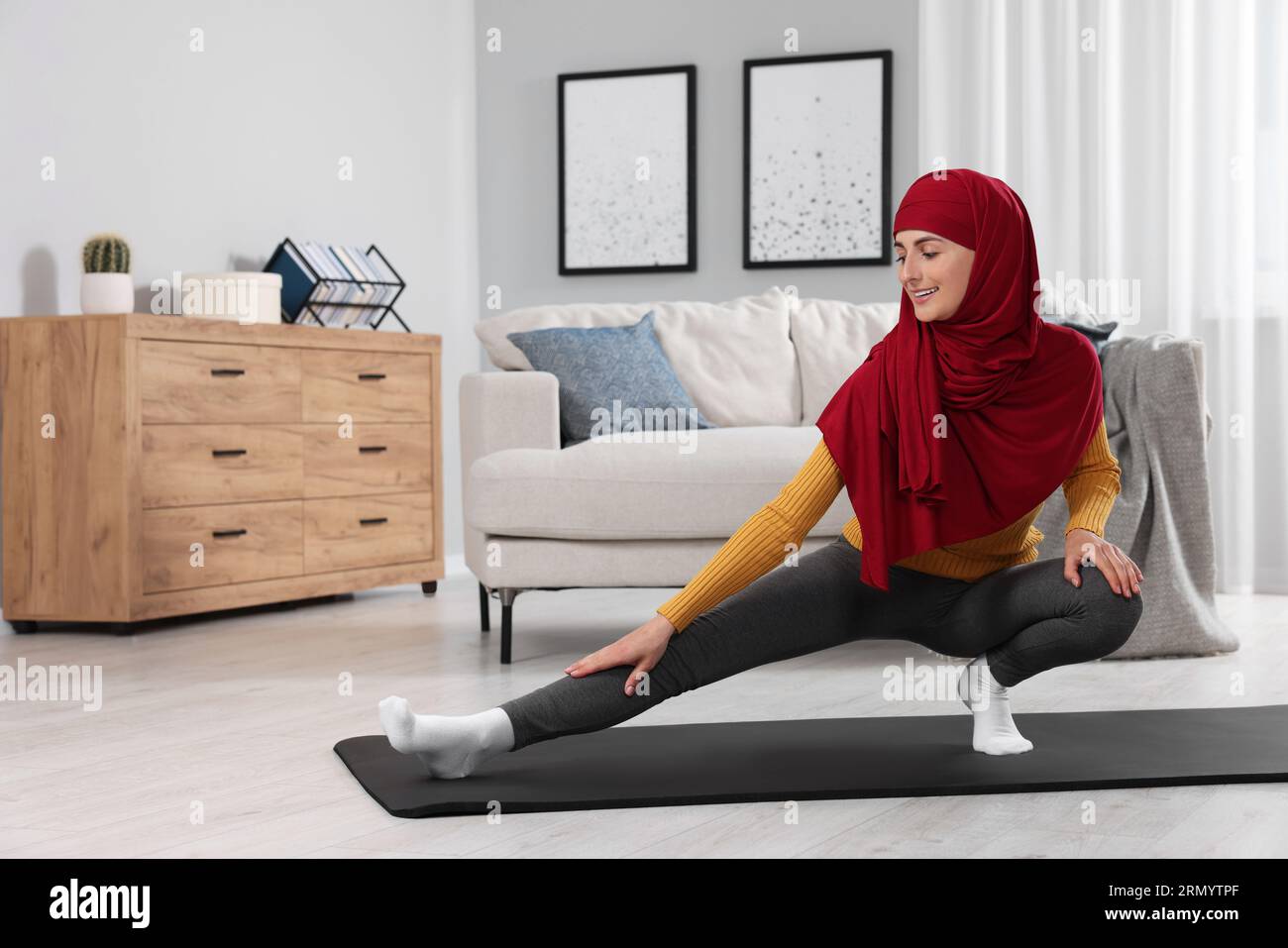 Muslim woman in hijab stretching on fitness mat at home. Space for text ...