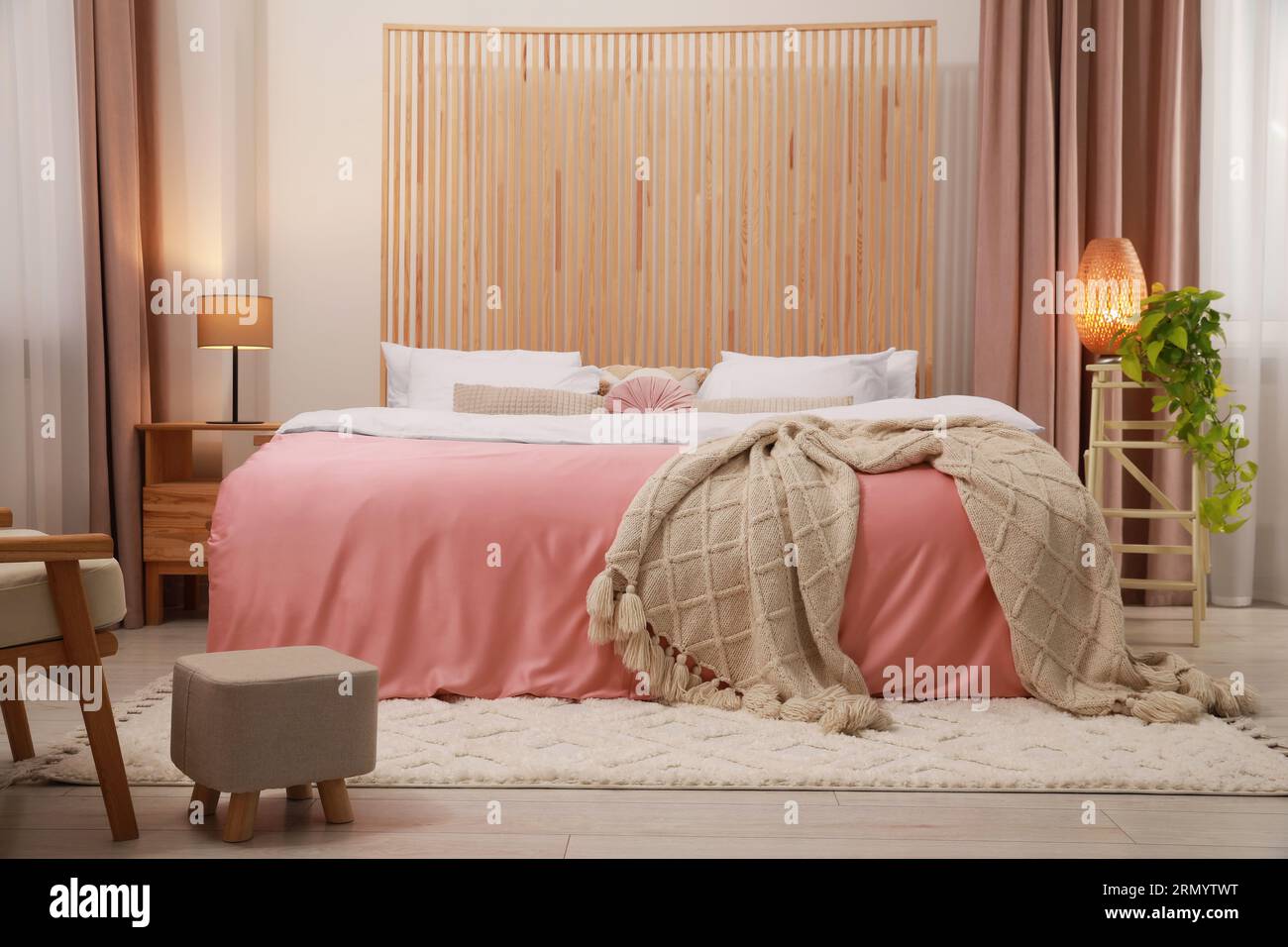 Stylish bedroom with comfortable bed, bedside table and ottoman ...