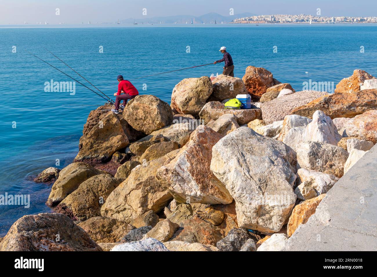 Two men fish off seaside boulders and a cat blends into the rocks below ...