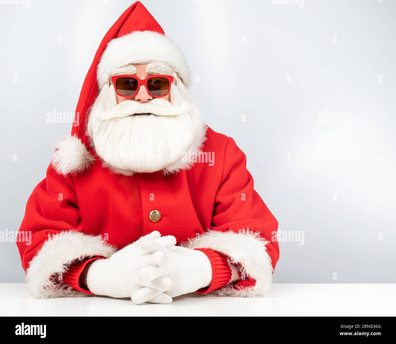 Portrait of santa claus sitting with his arms folded at a white table ...