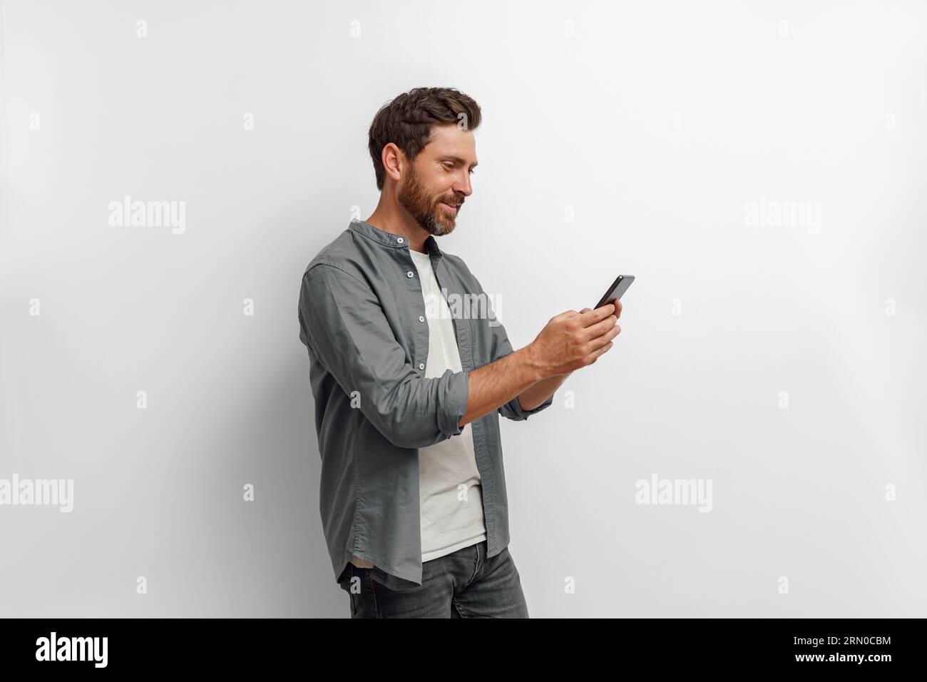 Smiling man looking to his mobile phone while standing on white ...