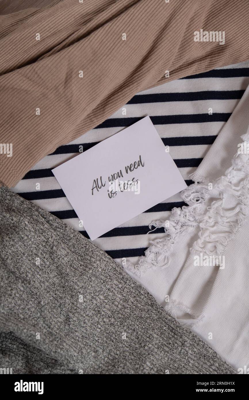 ALL YOU NEED IS LESS text on paper note on clothes assortment Second ...