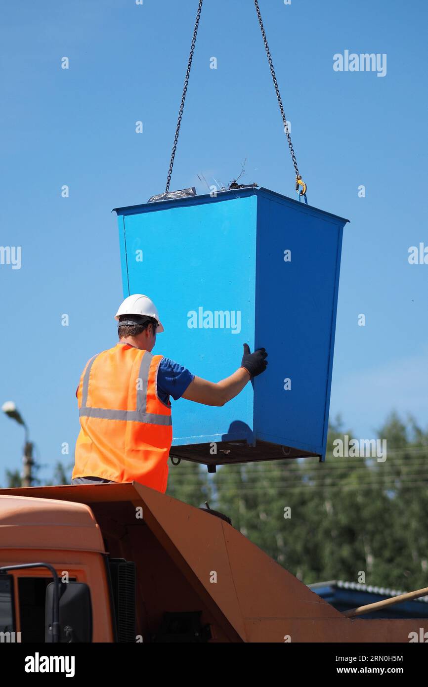 Handyman in protective vest and hard hat unloads garbage can into back ...