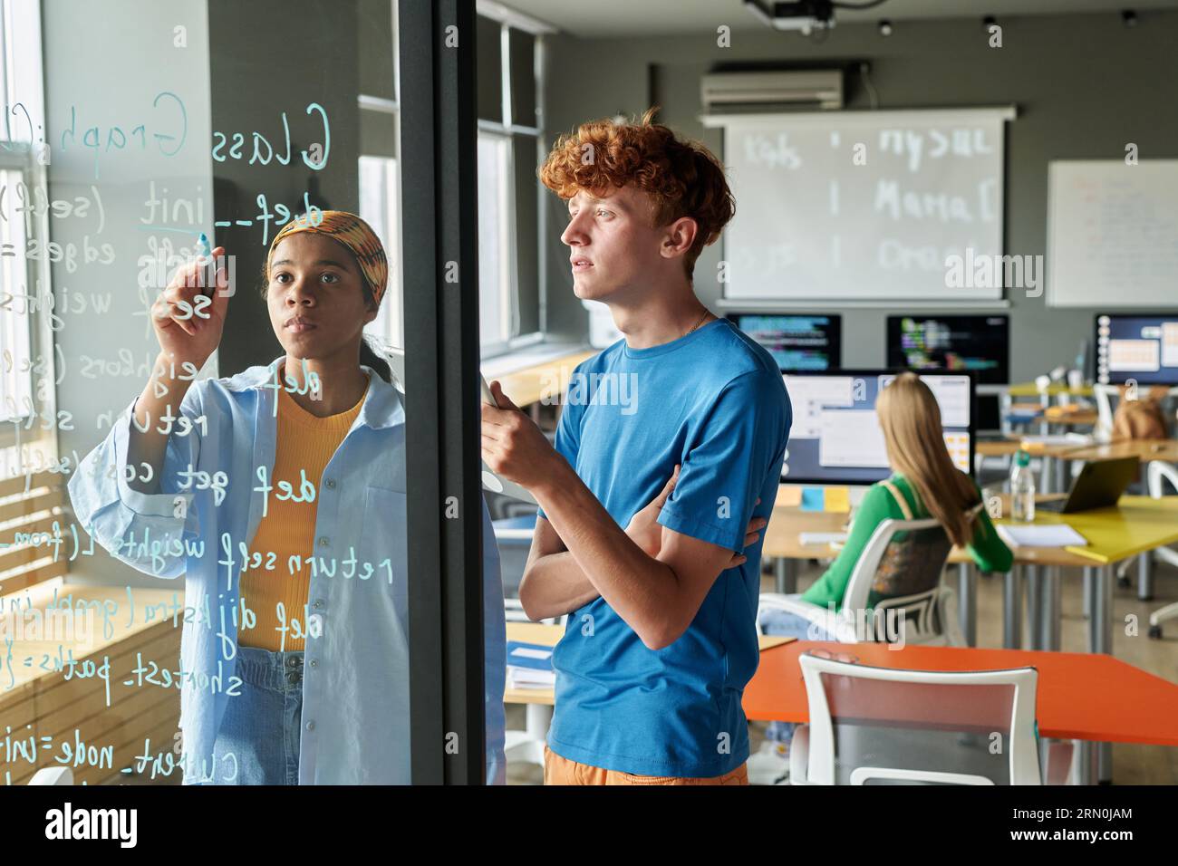 Couple of students writing formulas on glass wall and discussing it ...