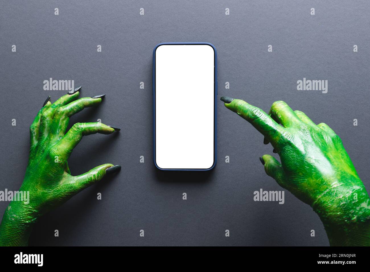 Green monster hands pointing on smartphone with copy space on grey ...