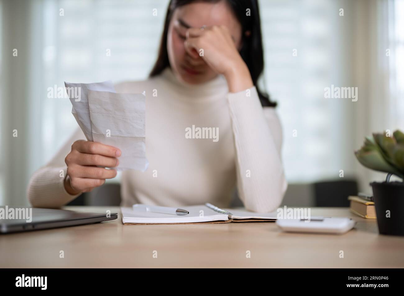 A stressed young Asian woman is holding invoices or bills, calculating ...