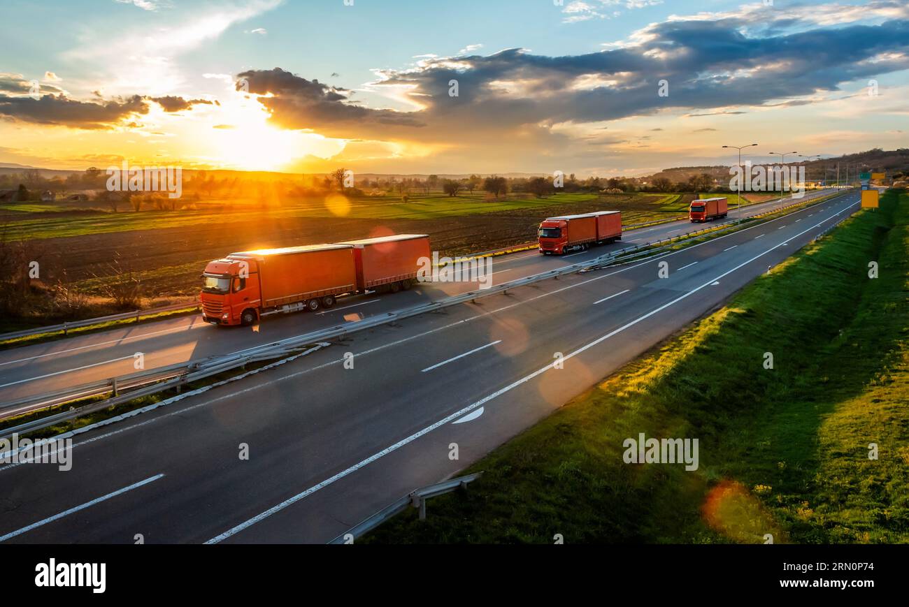 Three orange Transportation trucks with trailers on an asphalt highway ...